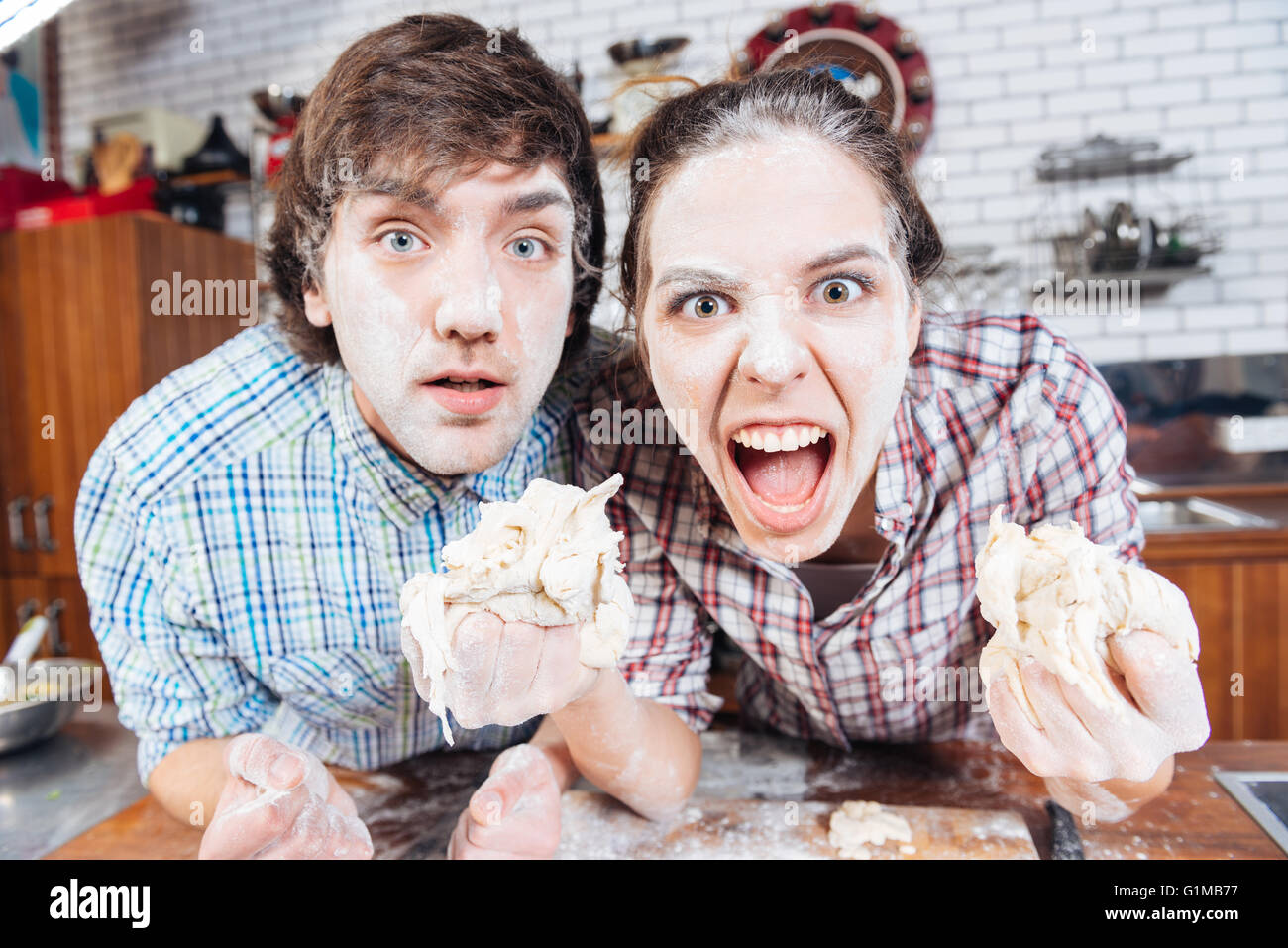 Comical angry young couple with flour on their faces holding dough and ...