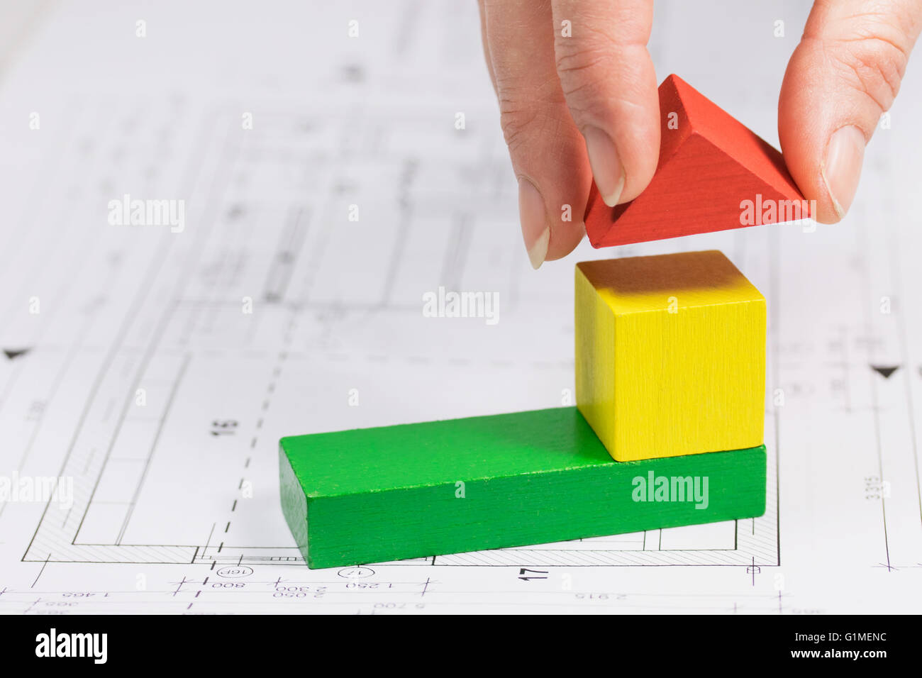 Woman's hand is building up colored house from wooden blocks and roofs ...