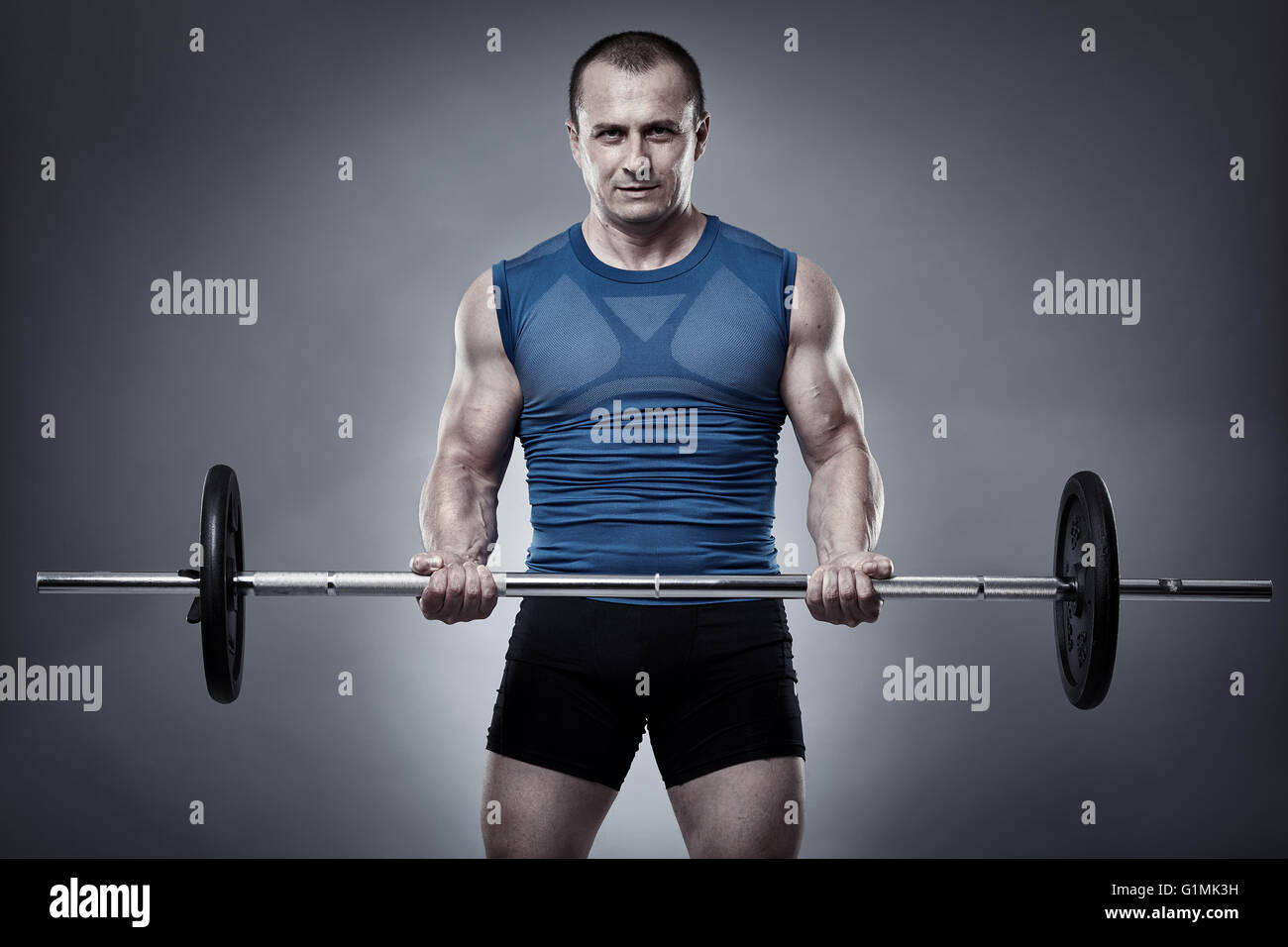 Man doing biceps curl with heavy barbell on gray background Stock Photo ...