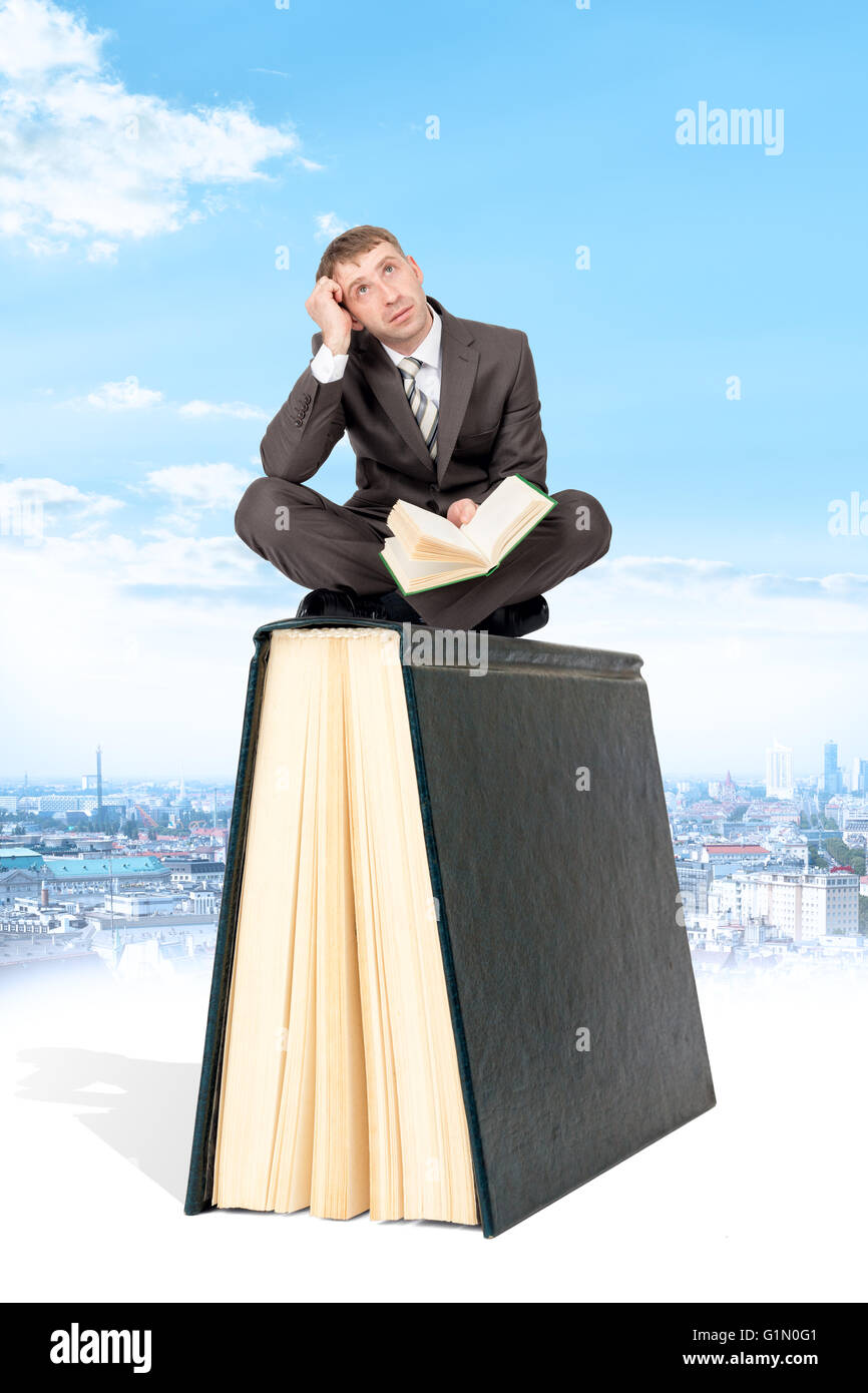 Man sitting on book and reading Stock Photo - Alamy