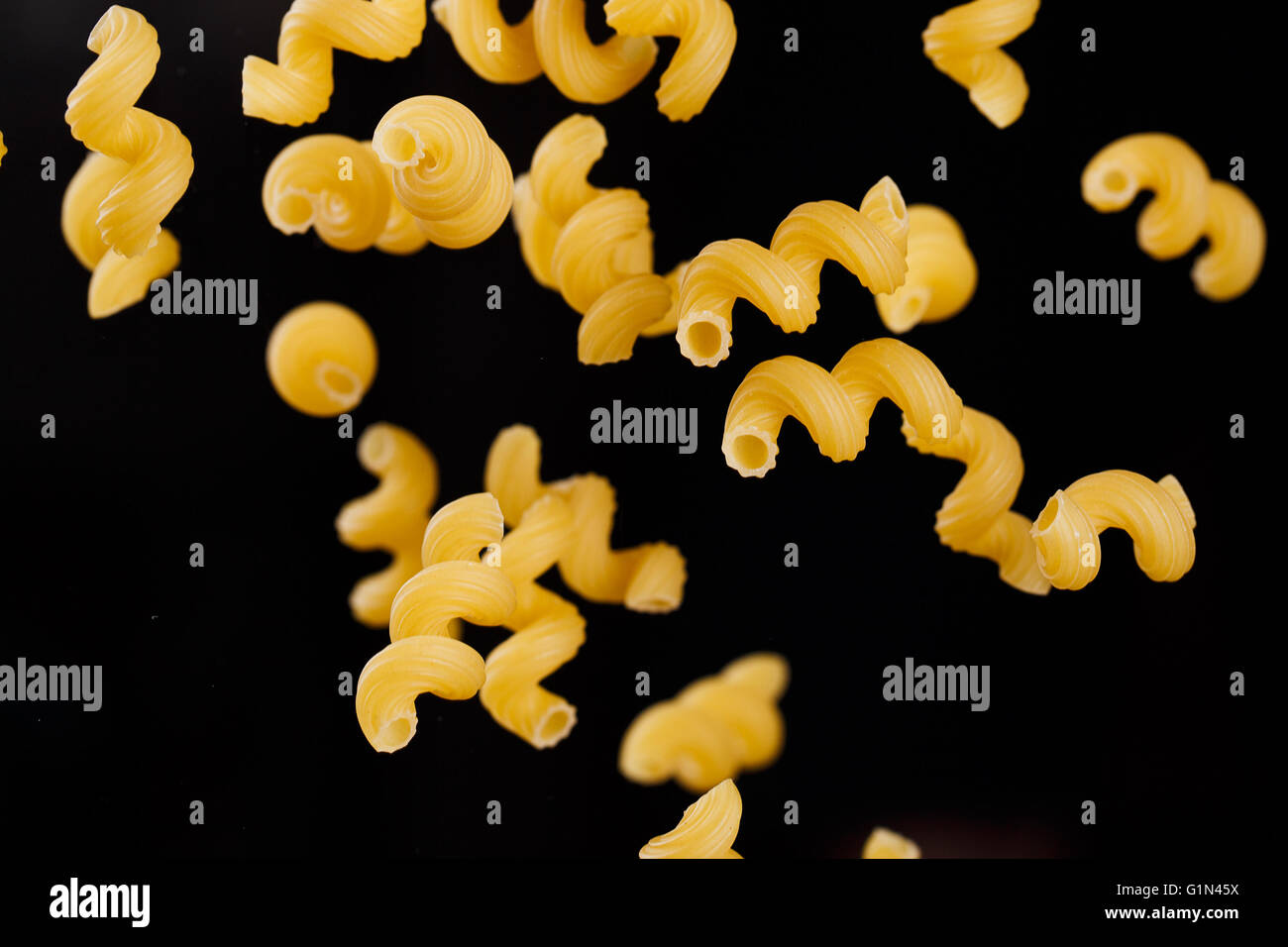 Falling cavatappi pasta. Flying yellow raw macaroni over black ...