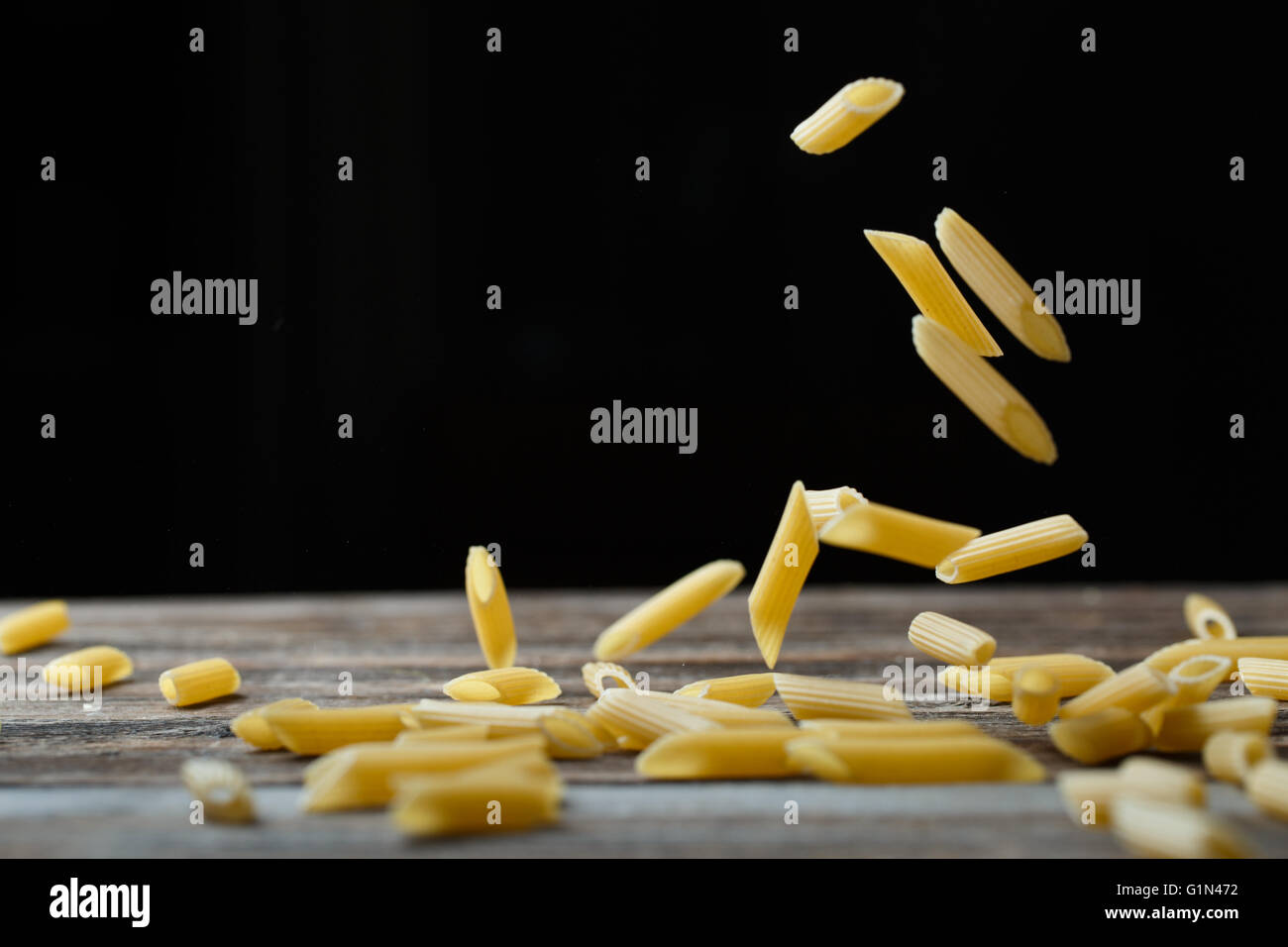 Falling penne pasta. Flying yellow raw macaroni over black background ...