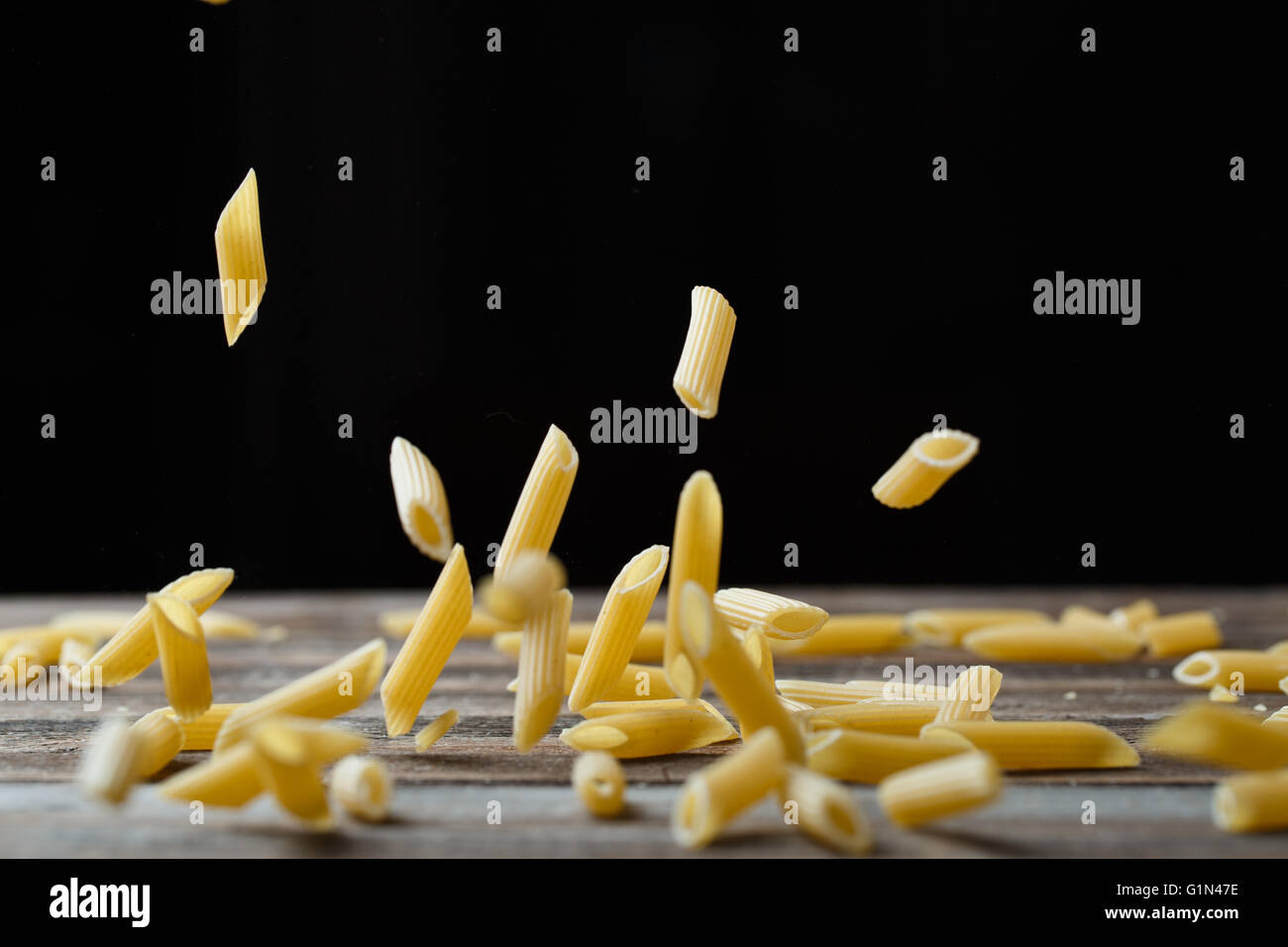 Falling penne pasta. Flying yellow raw macaroni over black background ...