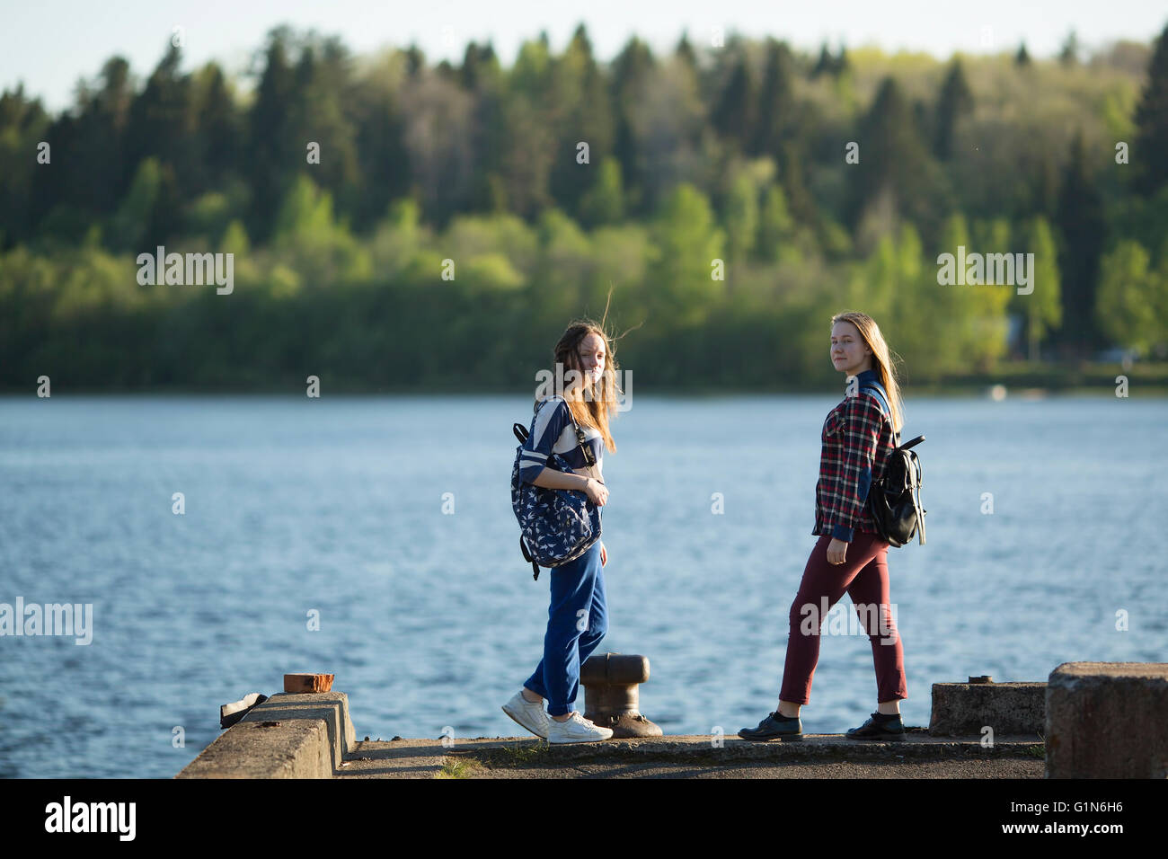 Two friends teen girls spend time together at the pier of the river ...