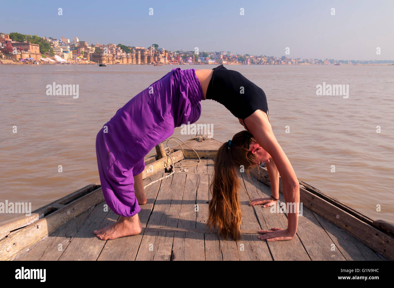 Young female practising yoga pose Urdhva Dhanurasana on the boat over Ganga river, India Stock ...
