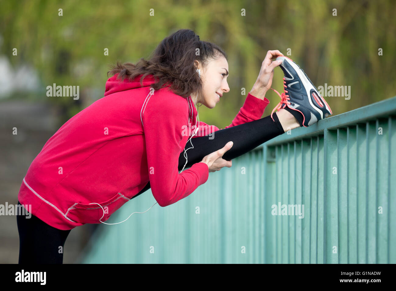 Portrait of sporty smiling woman doing hamstring stretch in park after ...
