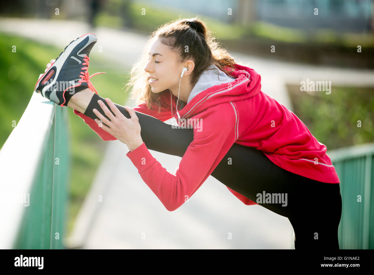 Profile portrait of sporty woman doing hamstring stretch in park after ...