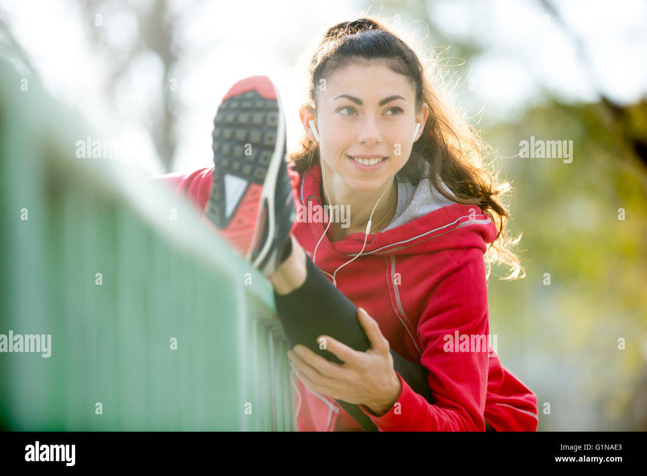 Portrait of sporty smiling woman doing hamstring stretch in park after ...