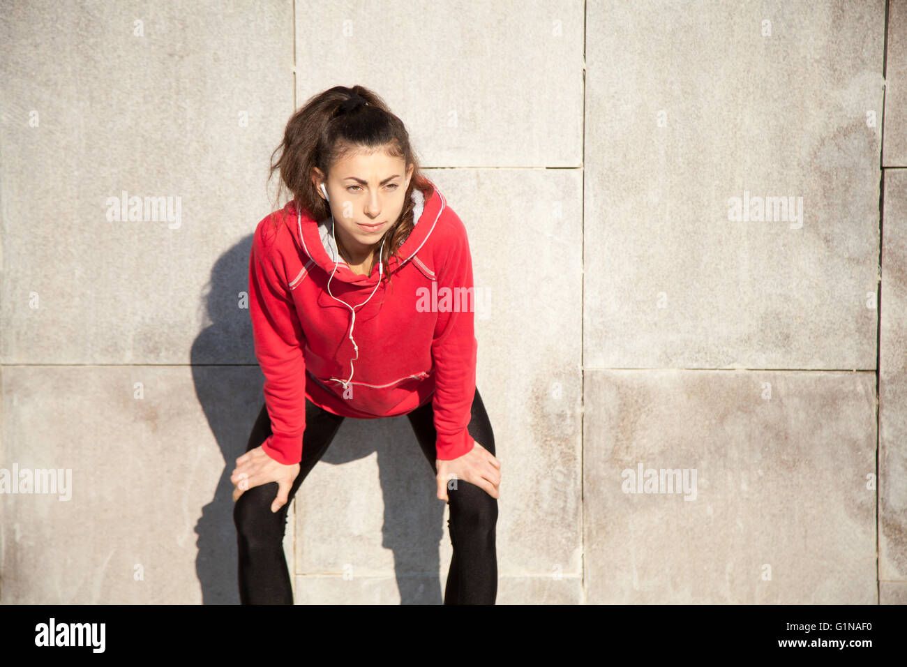 Portrait of young beautiful female leaning on gray wall while resting ...
