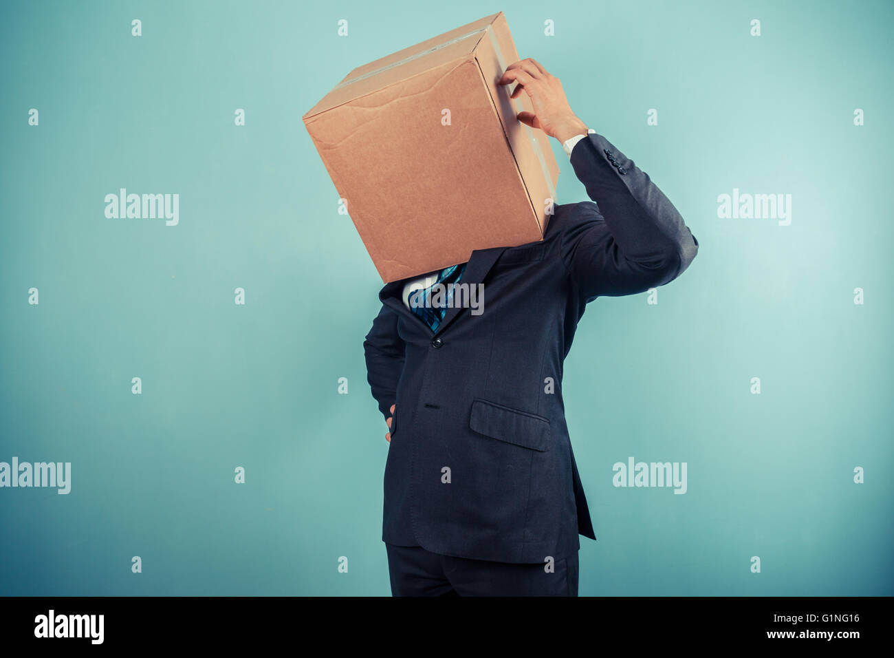 A businessman with a cardboard box on his head is scratching his head ...