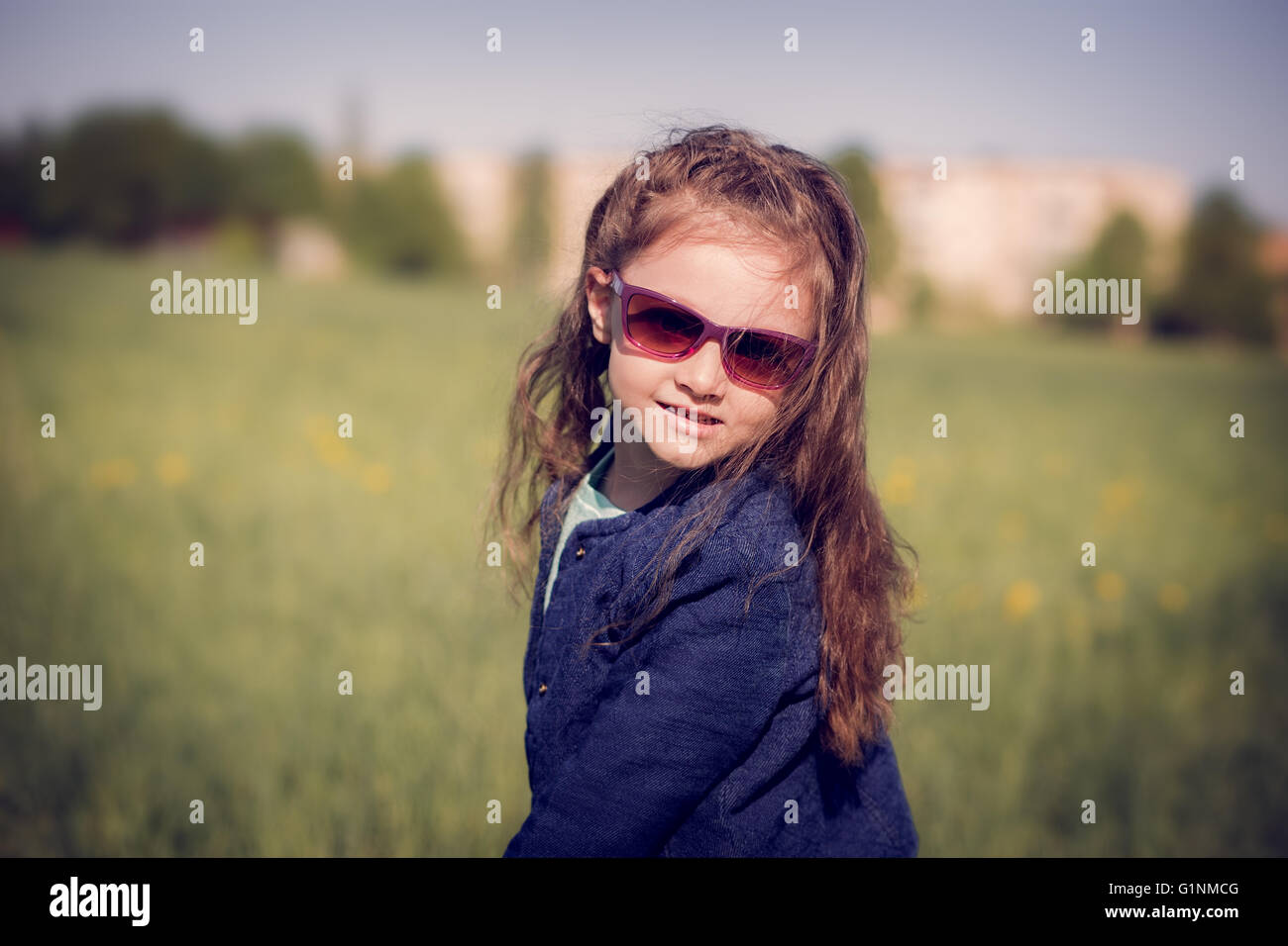 Fashion kid girl posing in blue jacket and sun glasses on spring nature ...