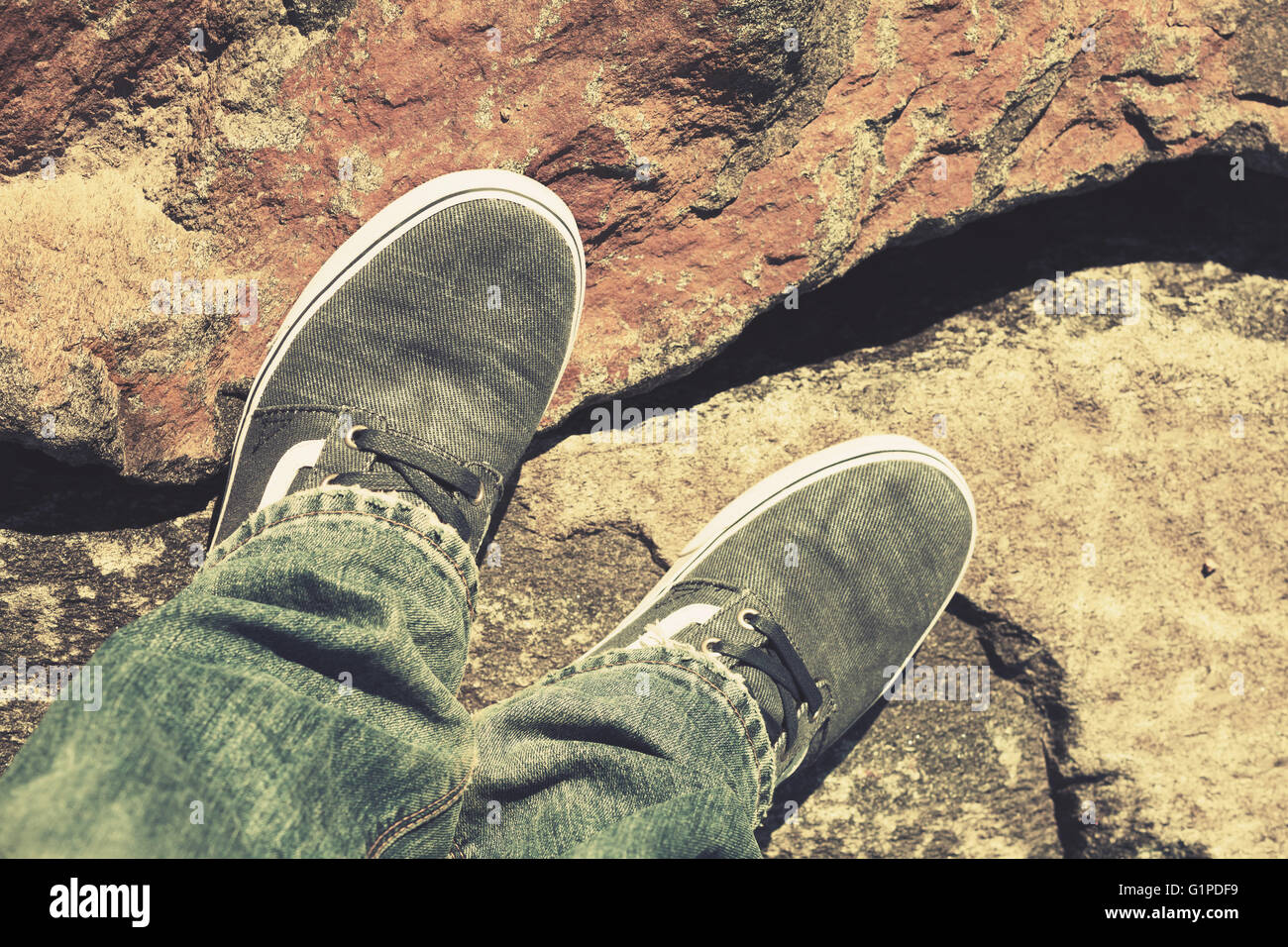 Male Feet In Canvas Shoes And Jeans Standing On Rough Rocky Ground