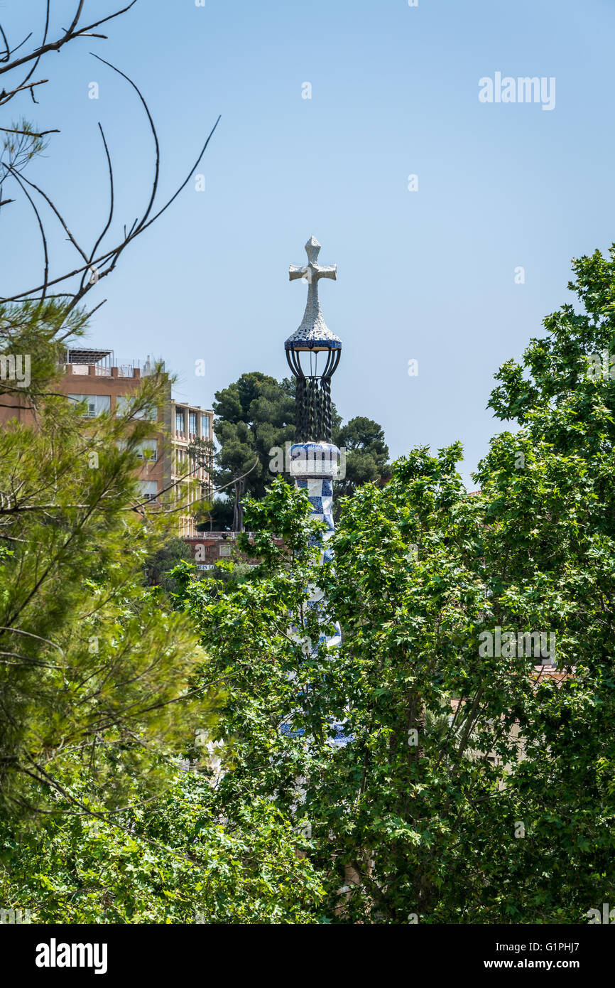 Iconic Gaudi cross peaking above trees in the world famous Park Güell ...