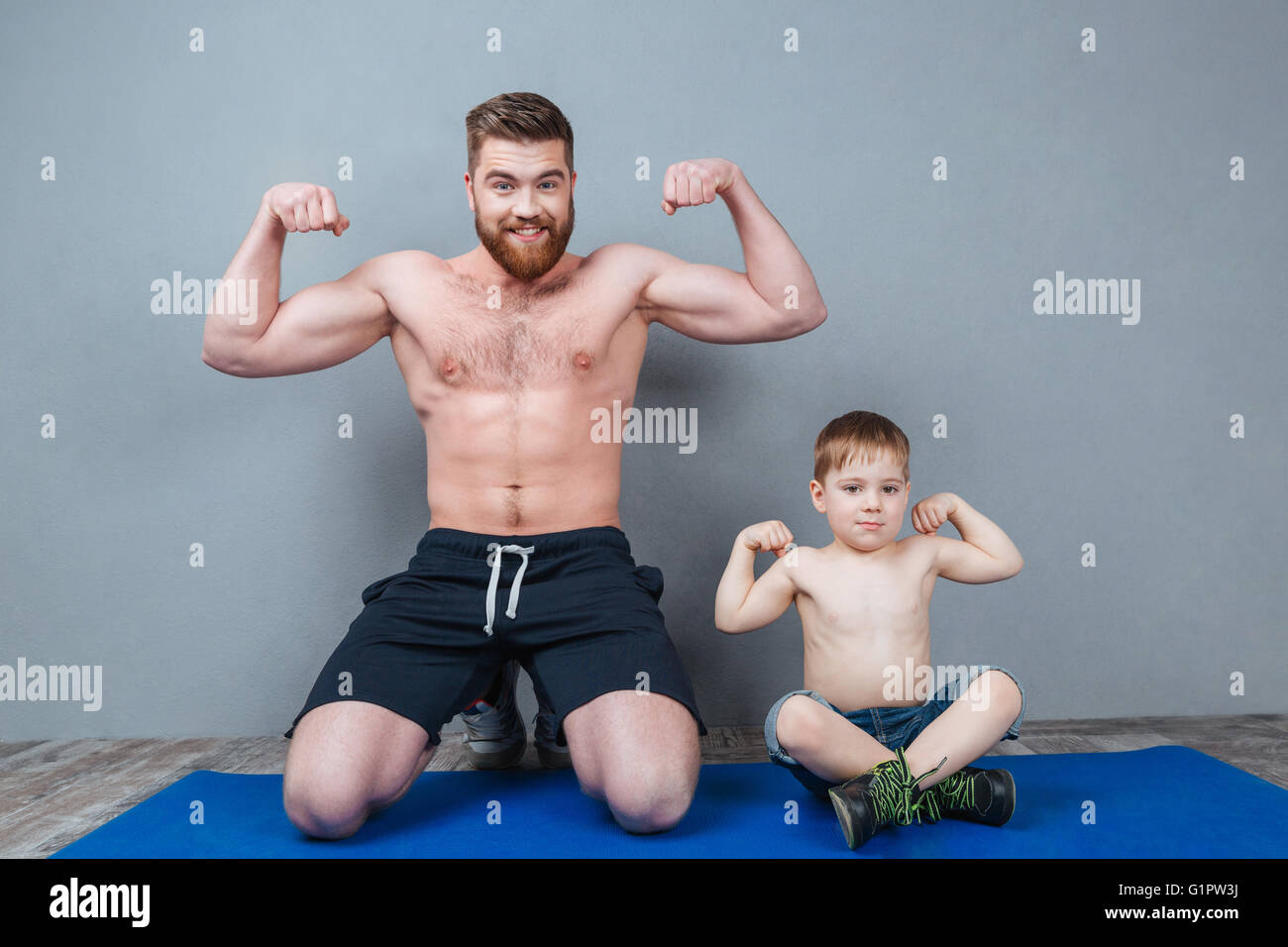 Cheerful handsome father and his little son sitting and showing biceps ...