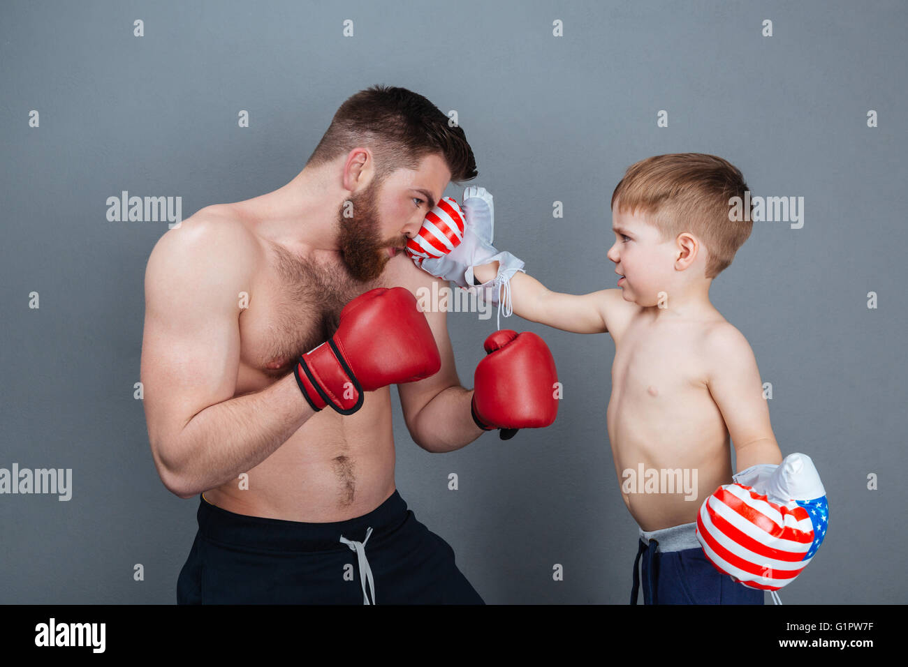 Dad and son playing using boxing gloves together over grey background ...