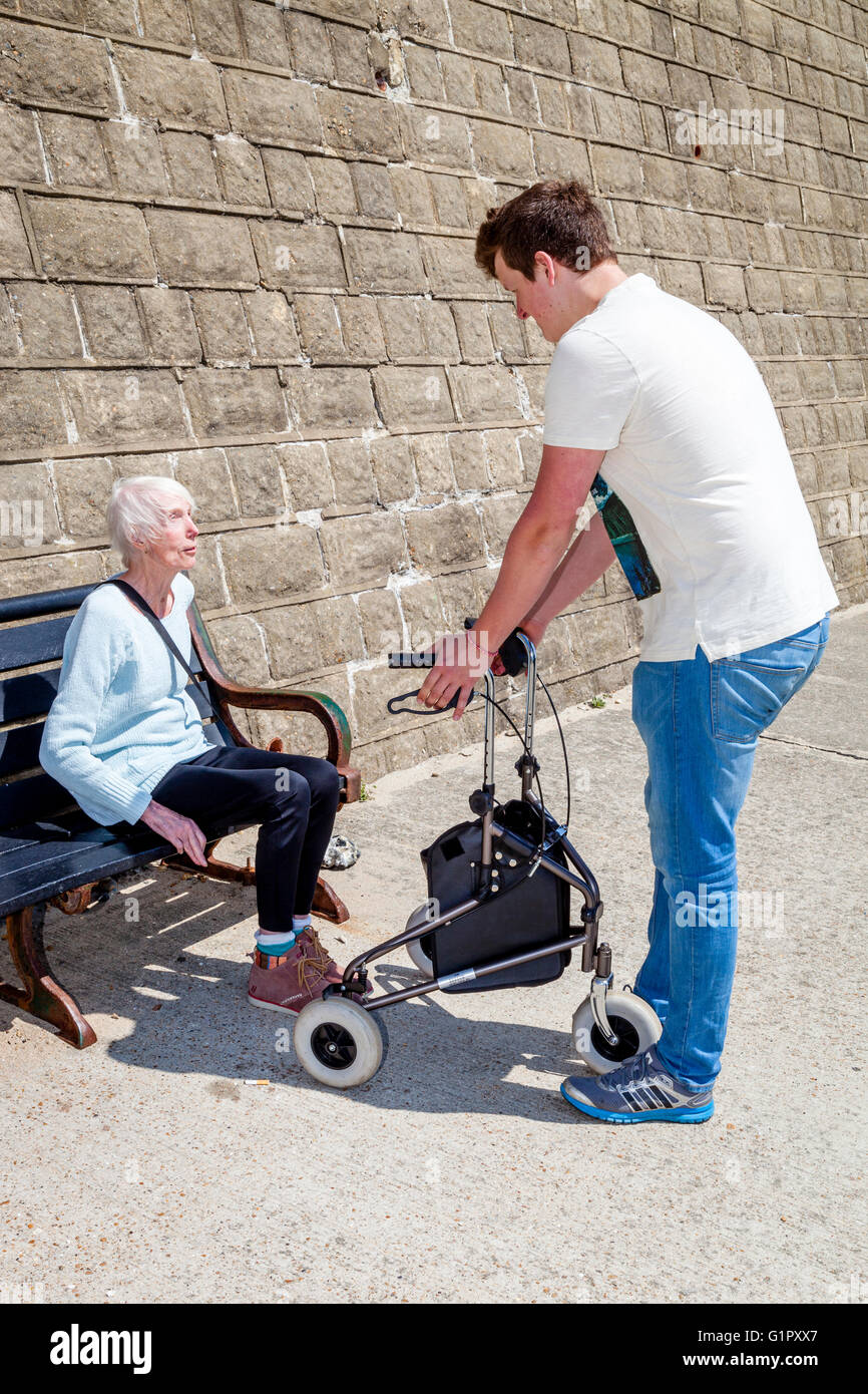 An Elderly Disabled Woman Getting Up From A Bench, Helped By Her ...