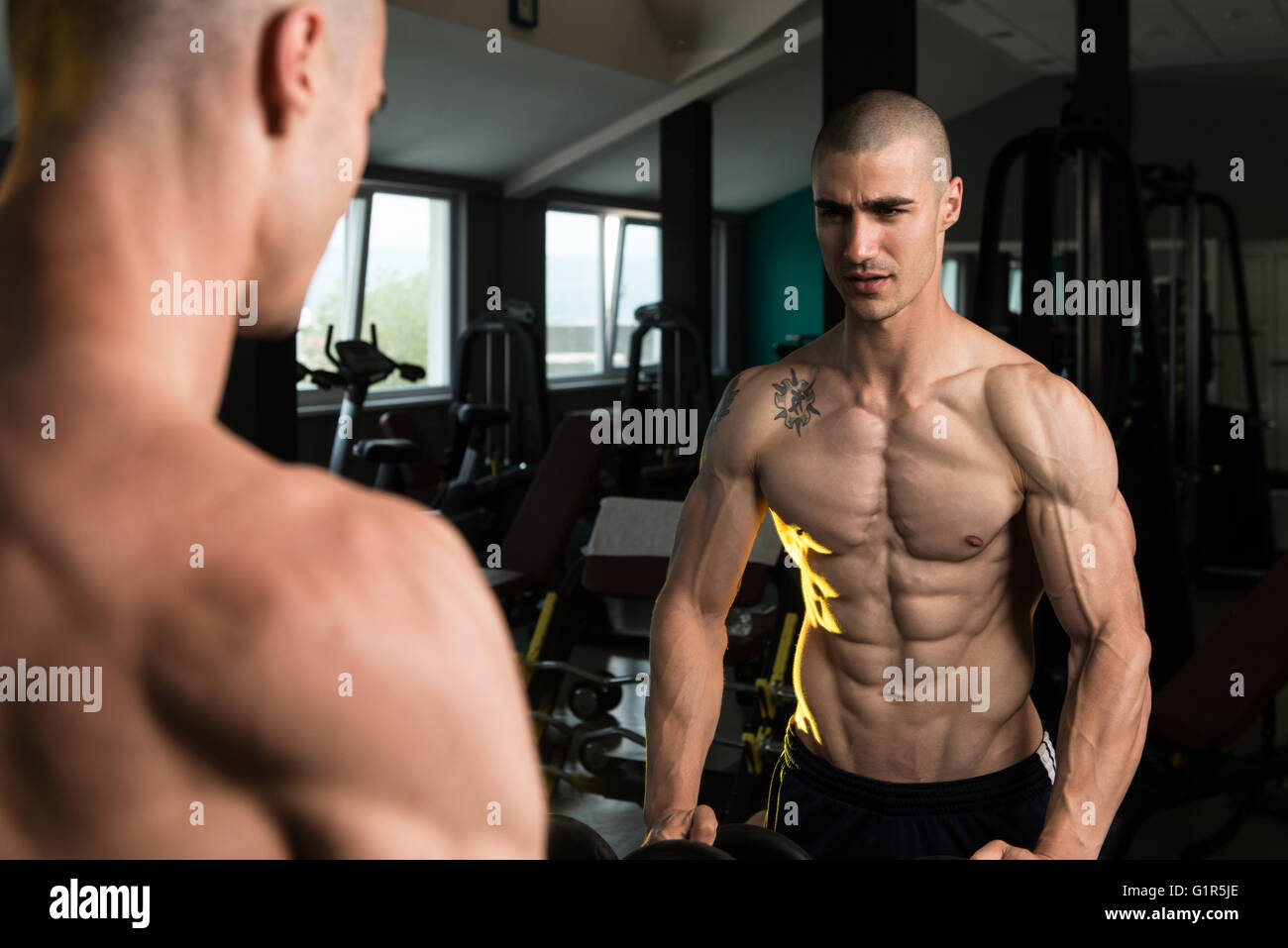 Young Man Standing Strong In Front Of A Mirror And Flexing Muscles ...