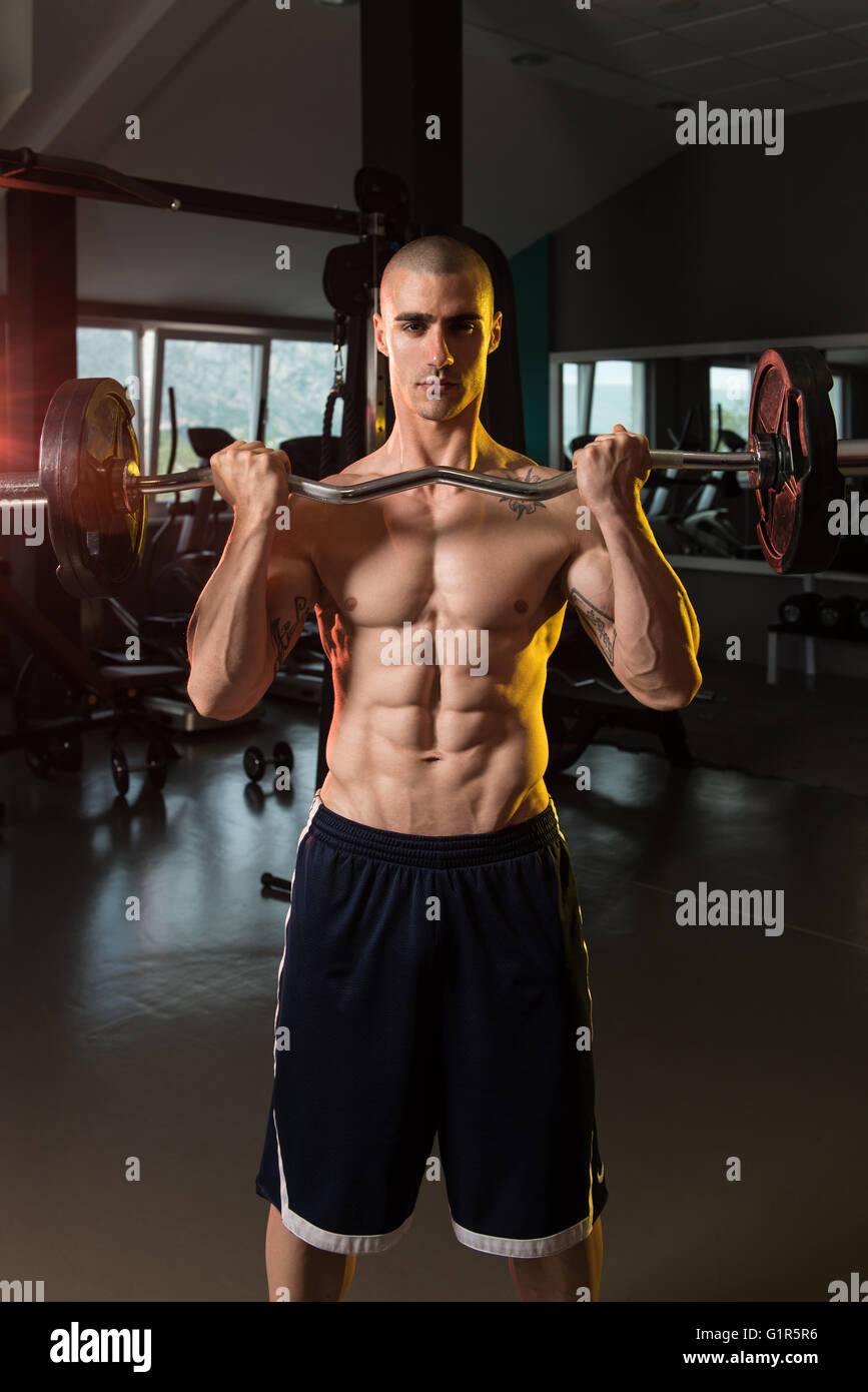Muscular Man Doing Heavy Weight Exercise For Biceps With Barbell In Gym ...