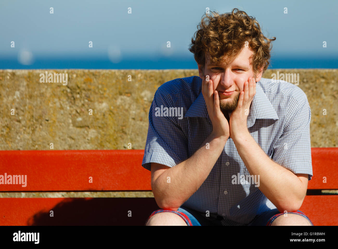 Tired exhausted man sitting on bench by sea ocean. Young guy relaxing ...