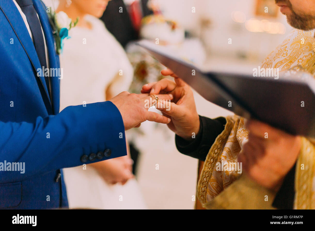The priest putting a ring on groom's finger during traditional wedding ...