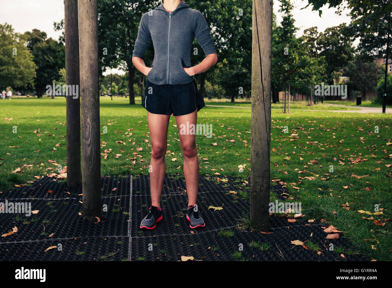 A young woman is standing by a set of pull up bars in the park Stock ...