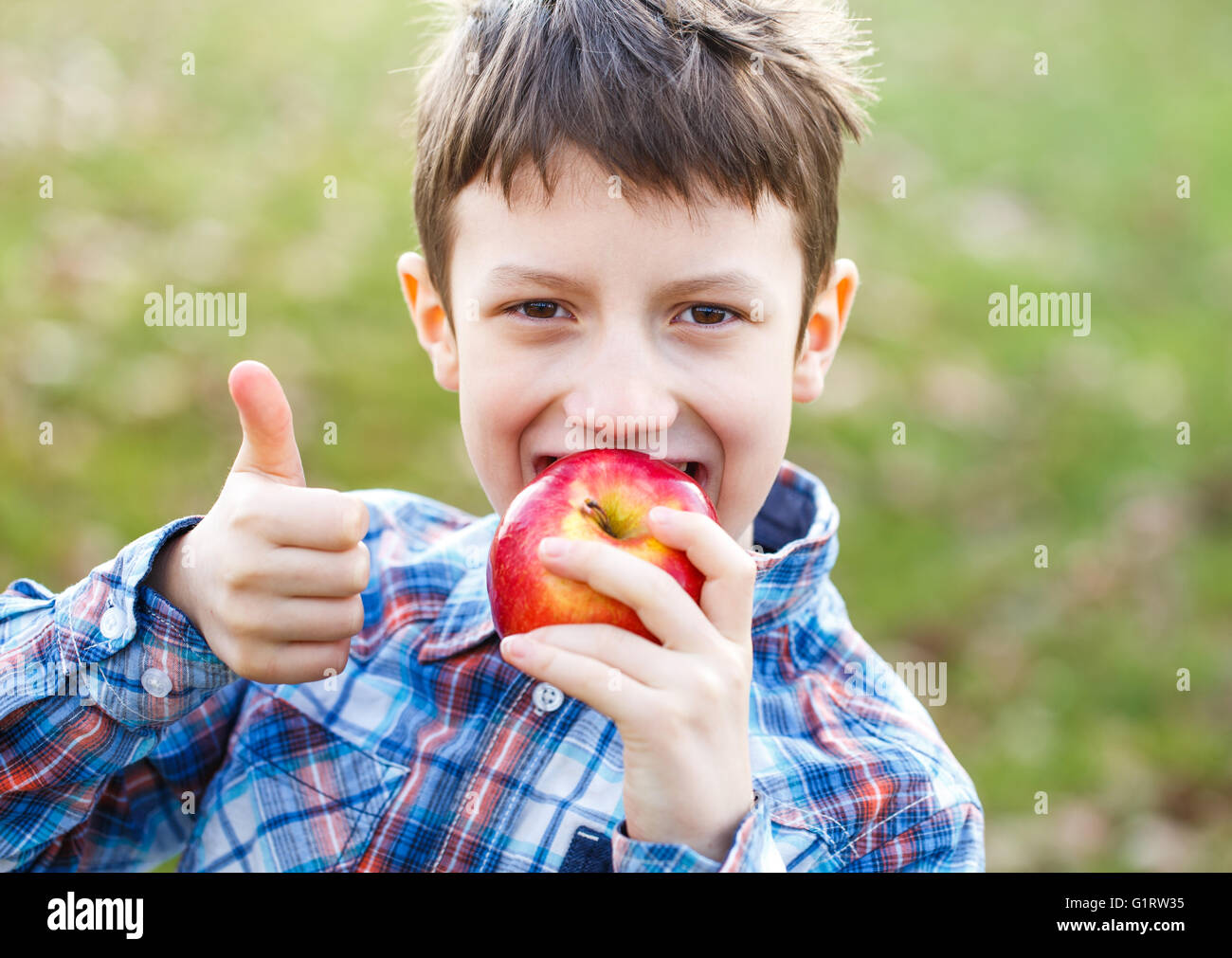 Happy little boy eating fresh red apple outdoor, thumb up Stock Photo ...