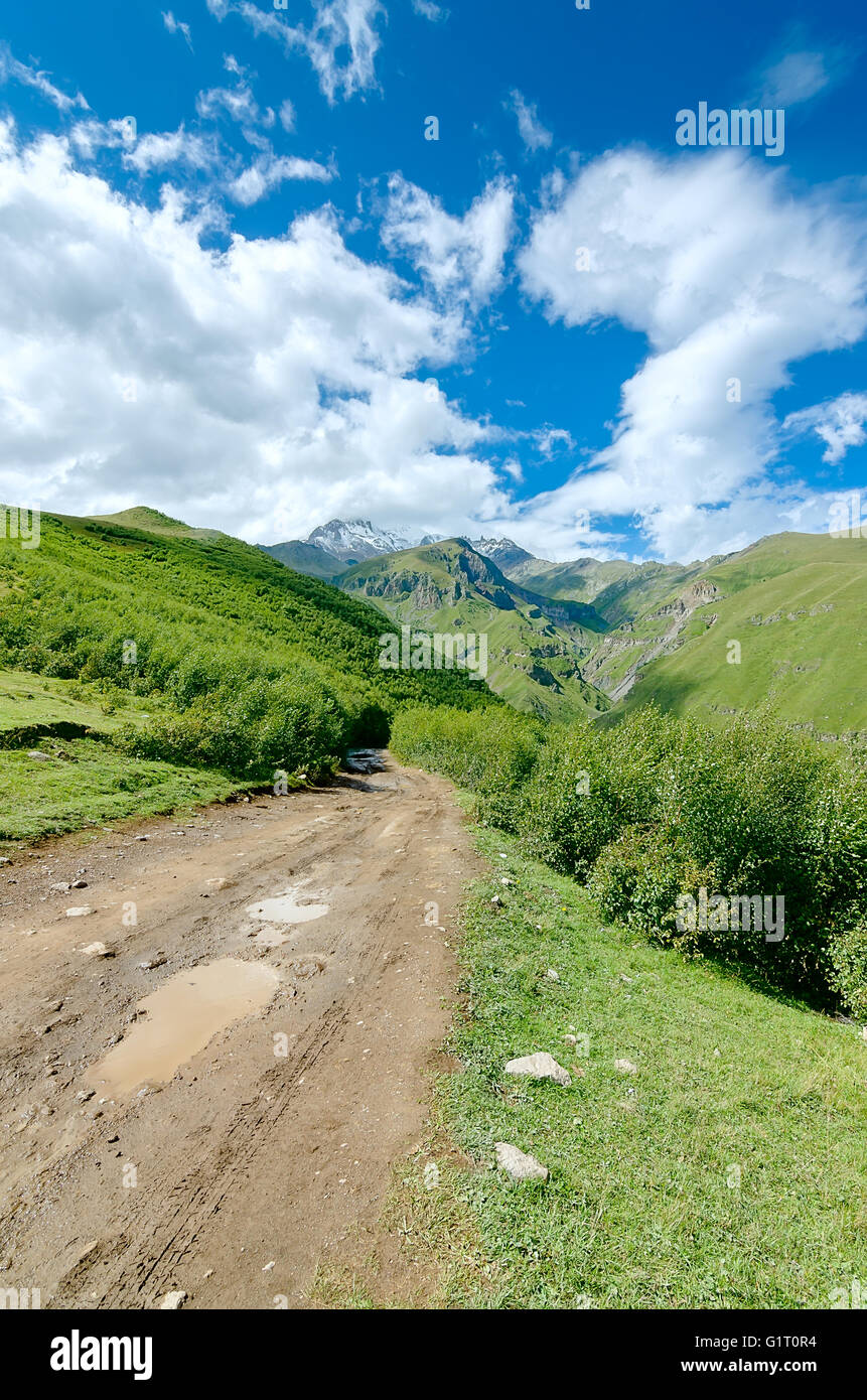 Road with tire tracks leading to mountains and beautiful clouds Stock ...