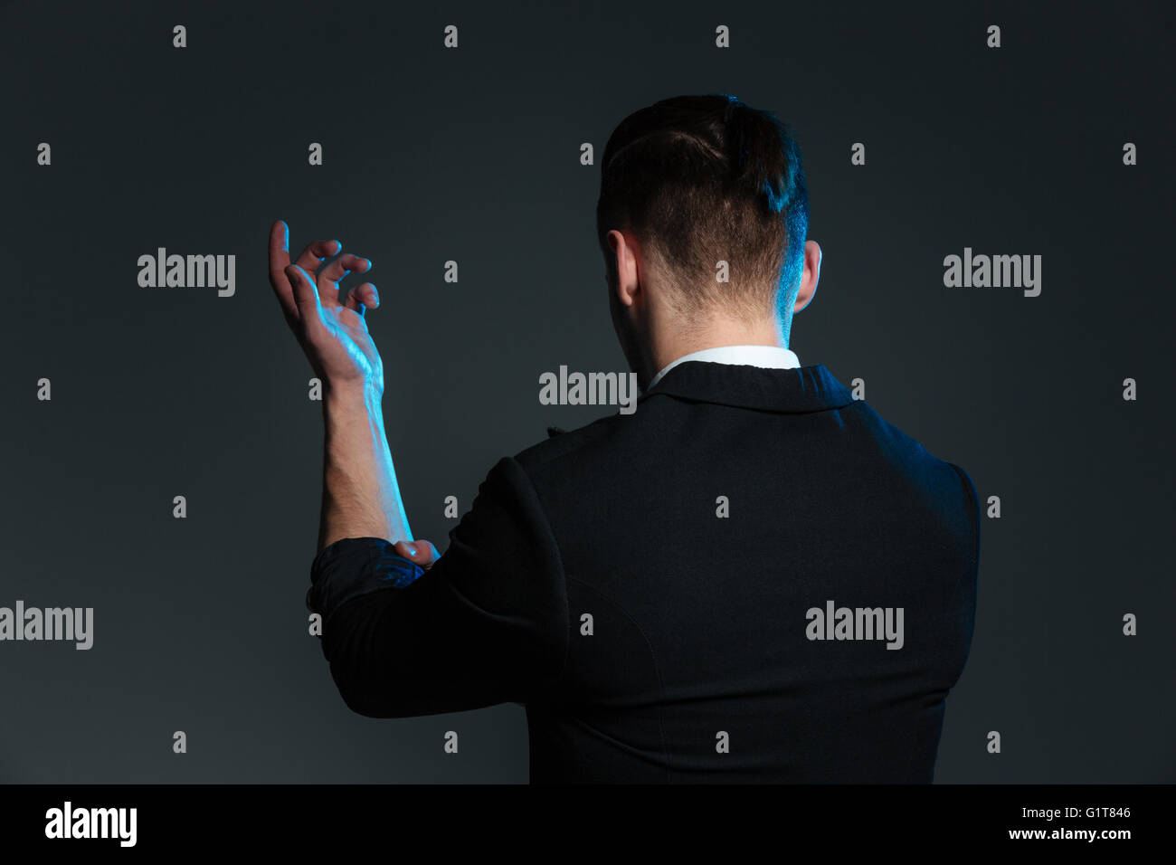 Back view of young man magician standing with raised hand over grey ...