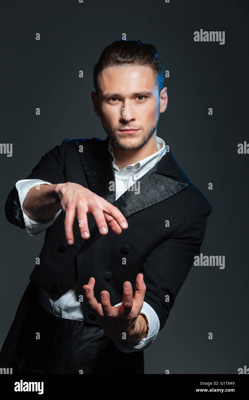 Handsome young man magician showing tricks over grey background Stock ...