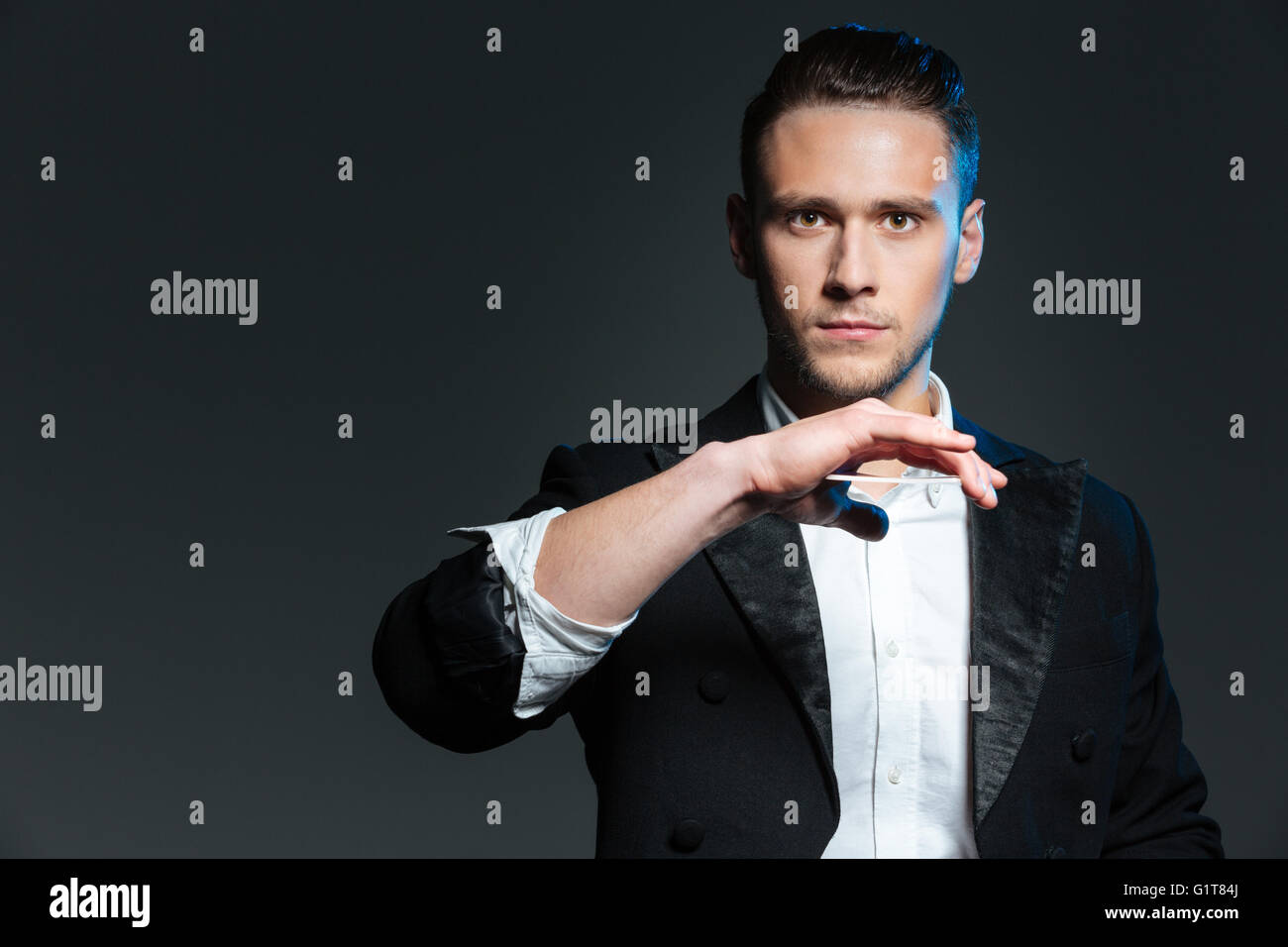 Handsome young man magician showing tricks with playing cards over grey ...