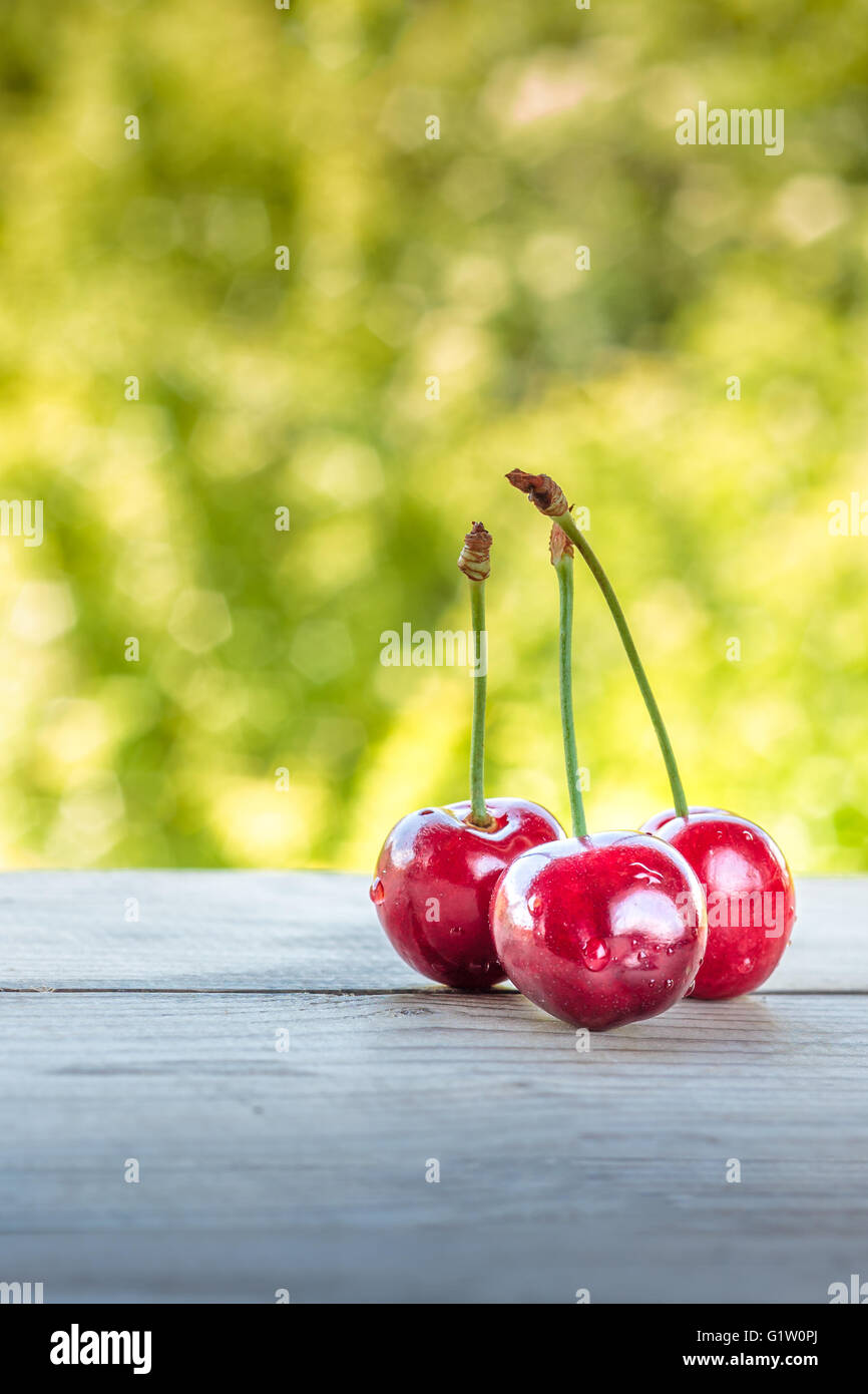 Three cherries with stems on wooden background. Plenty of copy space ...