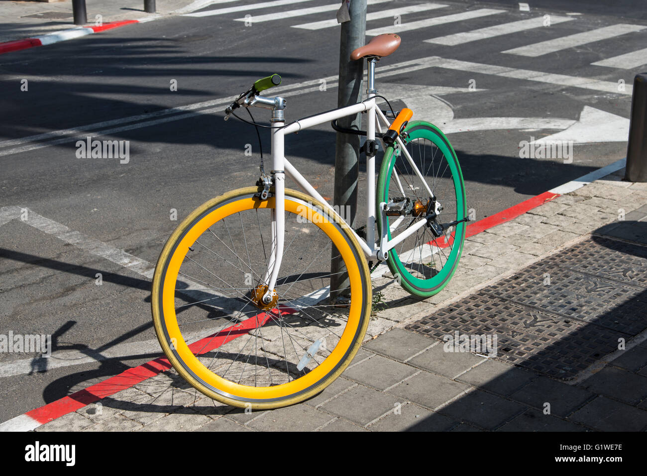 A colored bicycle locked to a post on the pavement Stock Photo - Alamy