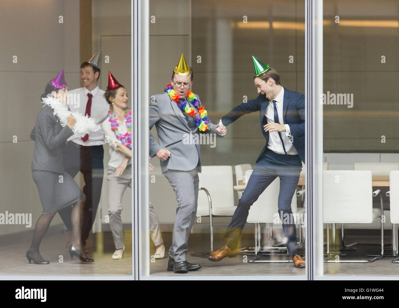 Playful business people in party hats dancing at conference room window ...