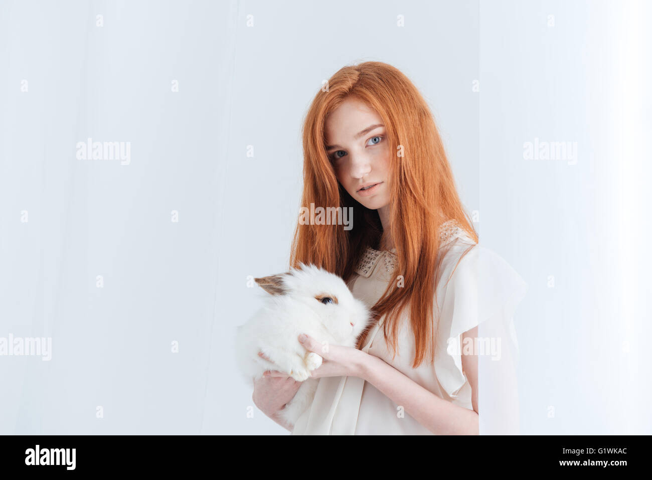 Attractive redhead woman holding rabbit isolated on a white background ...