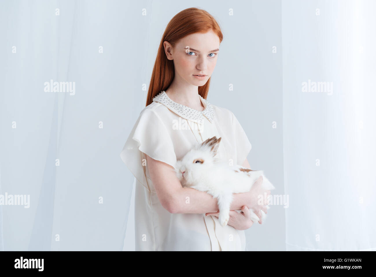 Serious redhead woman holding rabbit isolated on a white background ...