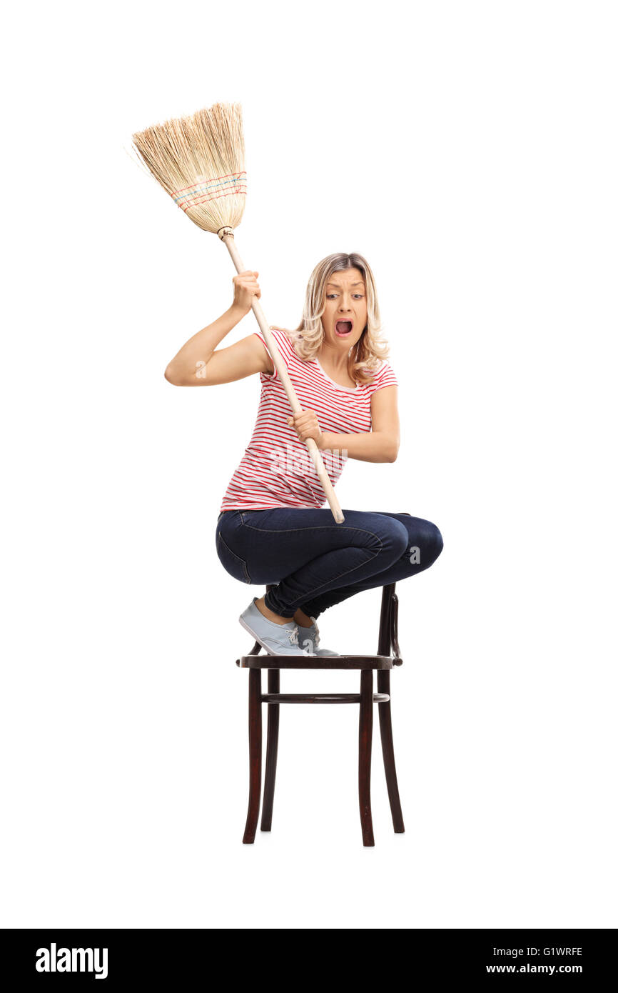 Vertical shot of a young scared woman swinging with a broom and chasing ...