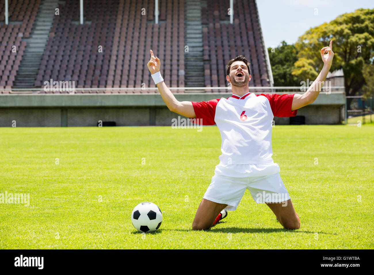 Excited football player kneeling in stadium Stock Photo - Alamy