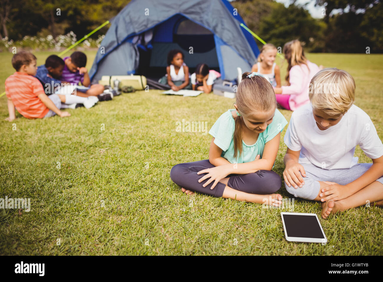 Smiling children are looking their tablet with other children behind ...