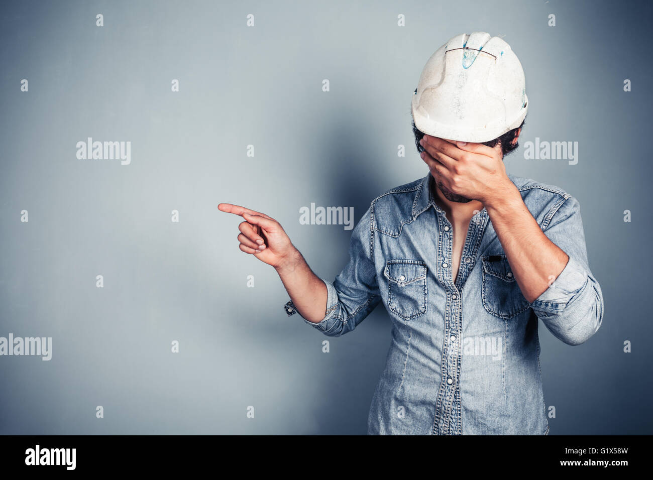 A blue collar worker covering his face is pointing Stock Photo - Alamy