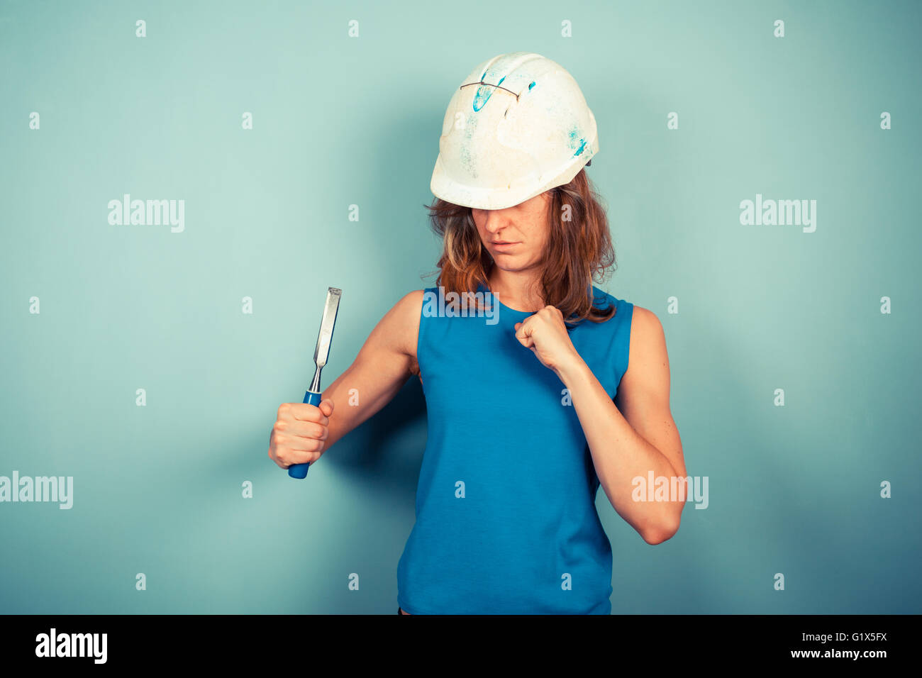 A young female builder is holding a chisel in an aggressive manner ...