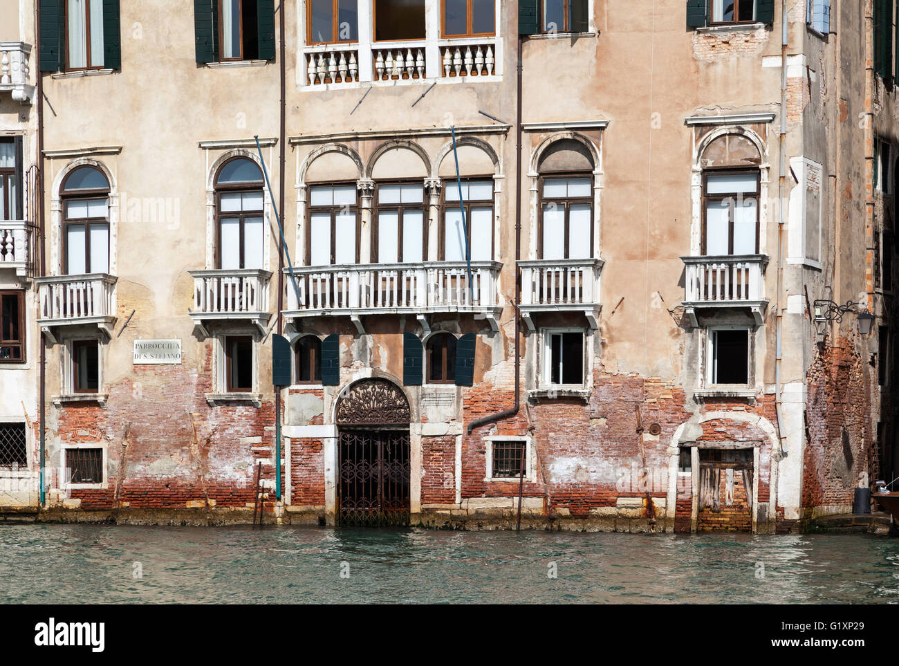 Sunlit crumbling building with a canal level water gate and white ...