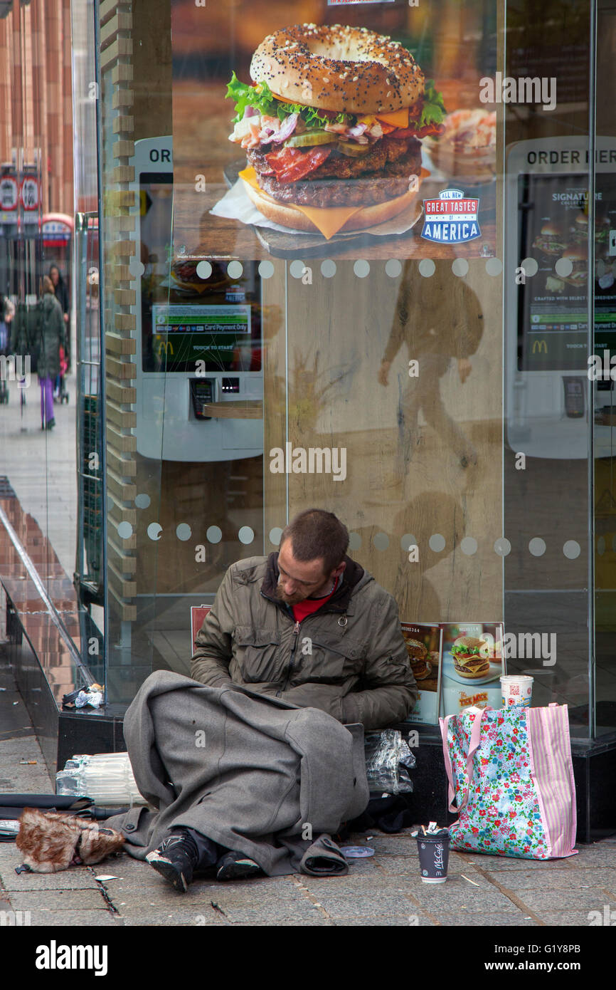 A homeless rough sleeper man seated in the pavement in poor condition ...