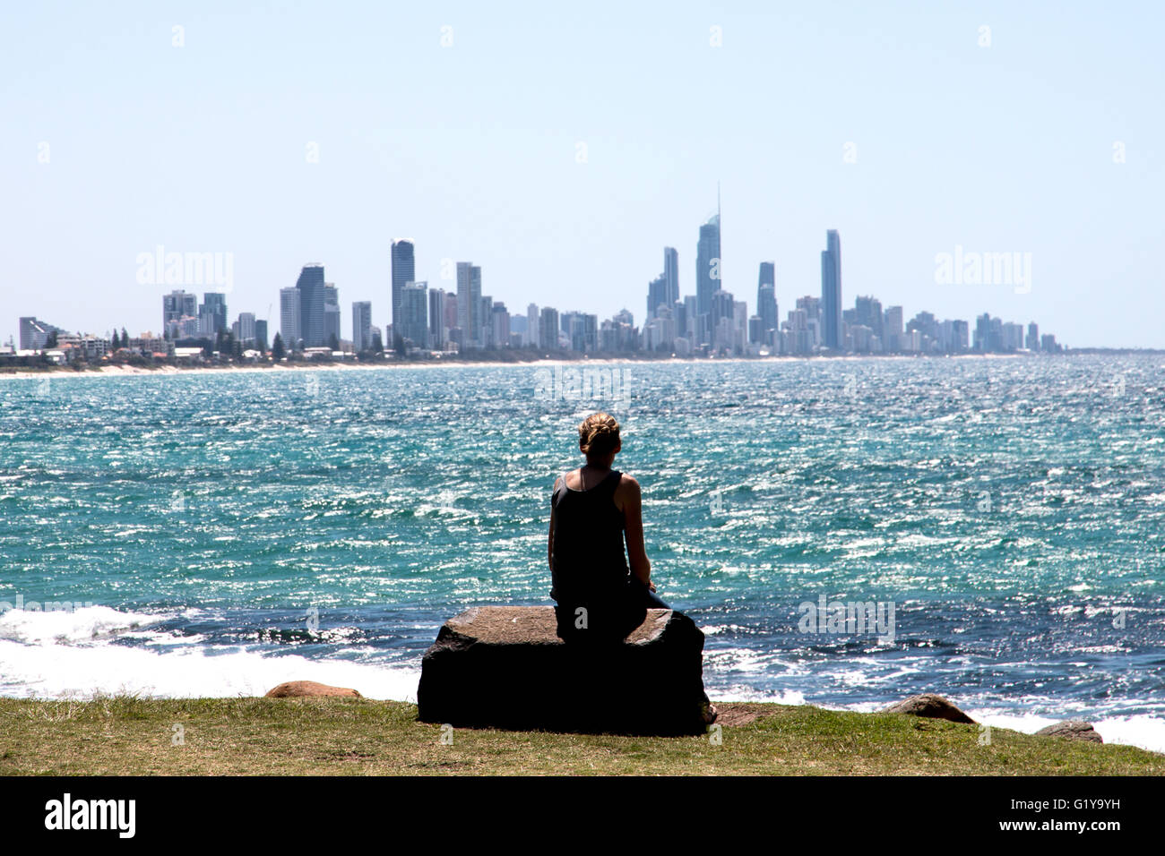 Woman sitting on rock looking across to the high rise buildings of the ...