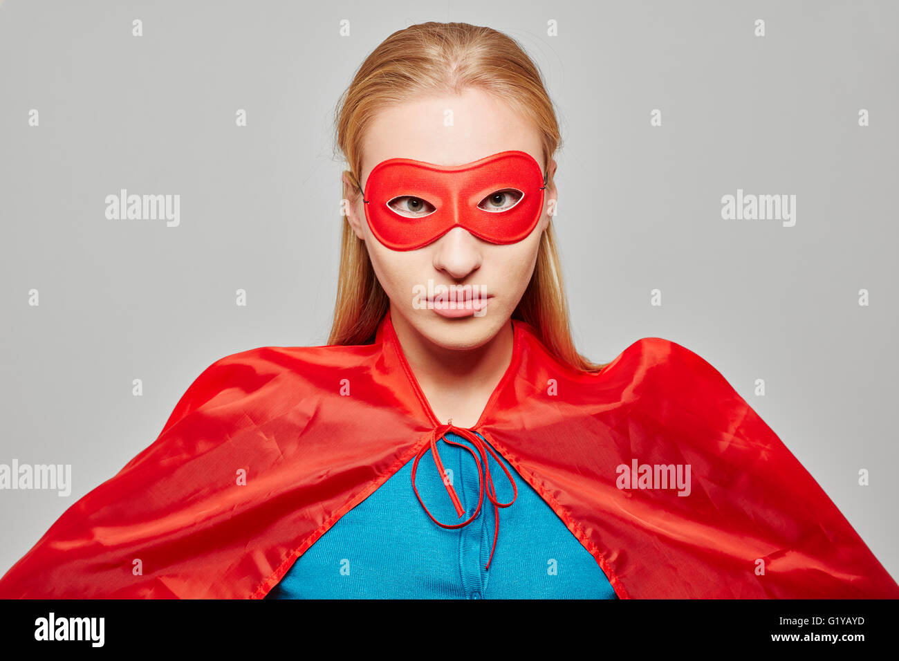Young blond woman dressed as a superhero with a mask and a cape looking ...