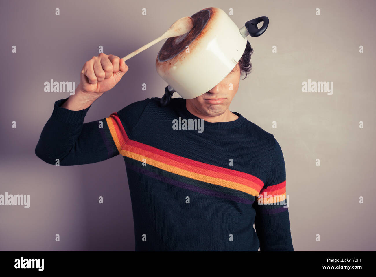 A silly young man is wearing a cooking pot on his had and is holding a ...