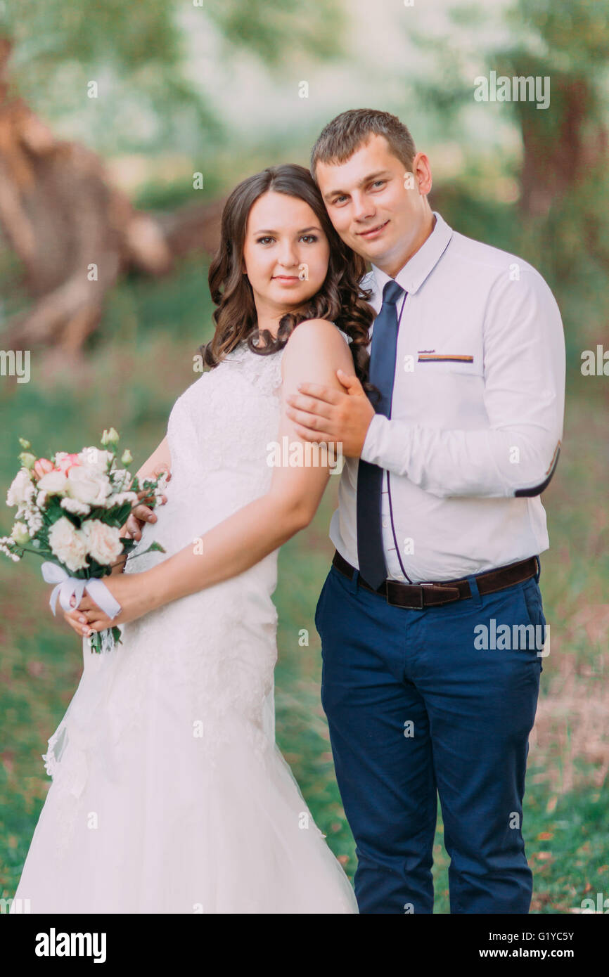 Pretty bride with bridal bouquet and groom posing looking at camera on ...