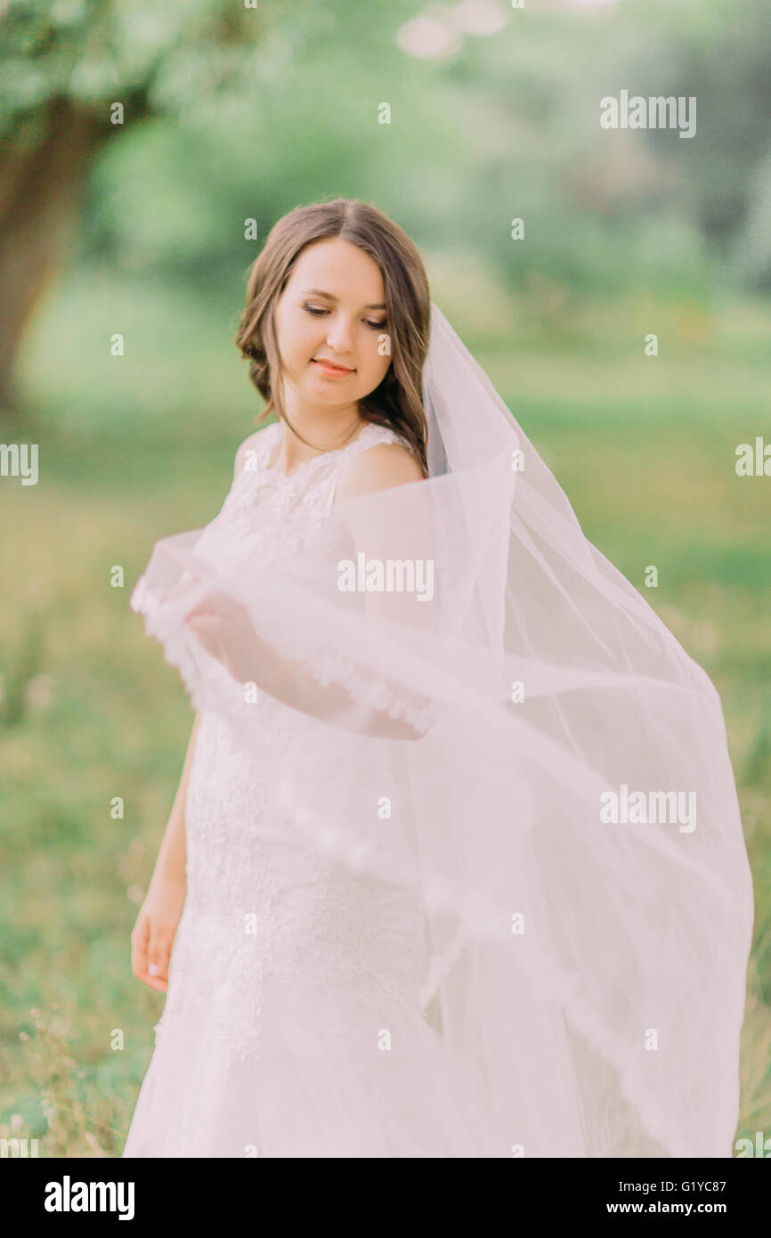 Beautiful bride in white dress playing with veil, spring green park on ...