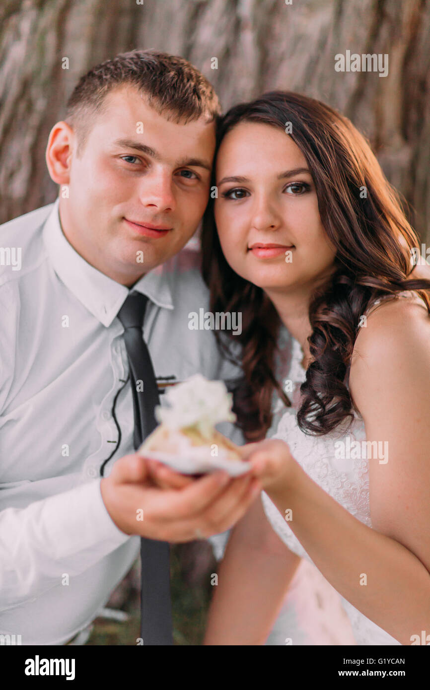 Bride and groom looking at camera holding piece of their wedding cake ...