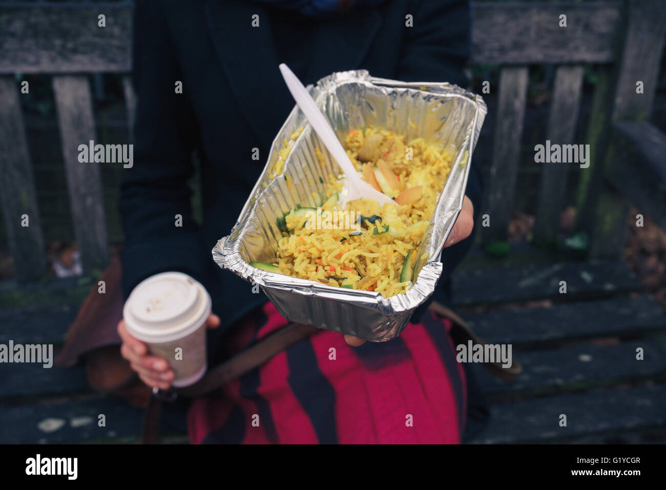 A woman i sitting on a bench and is holding a container of indian food ...