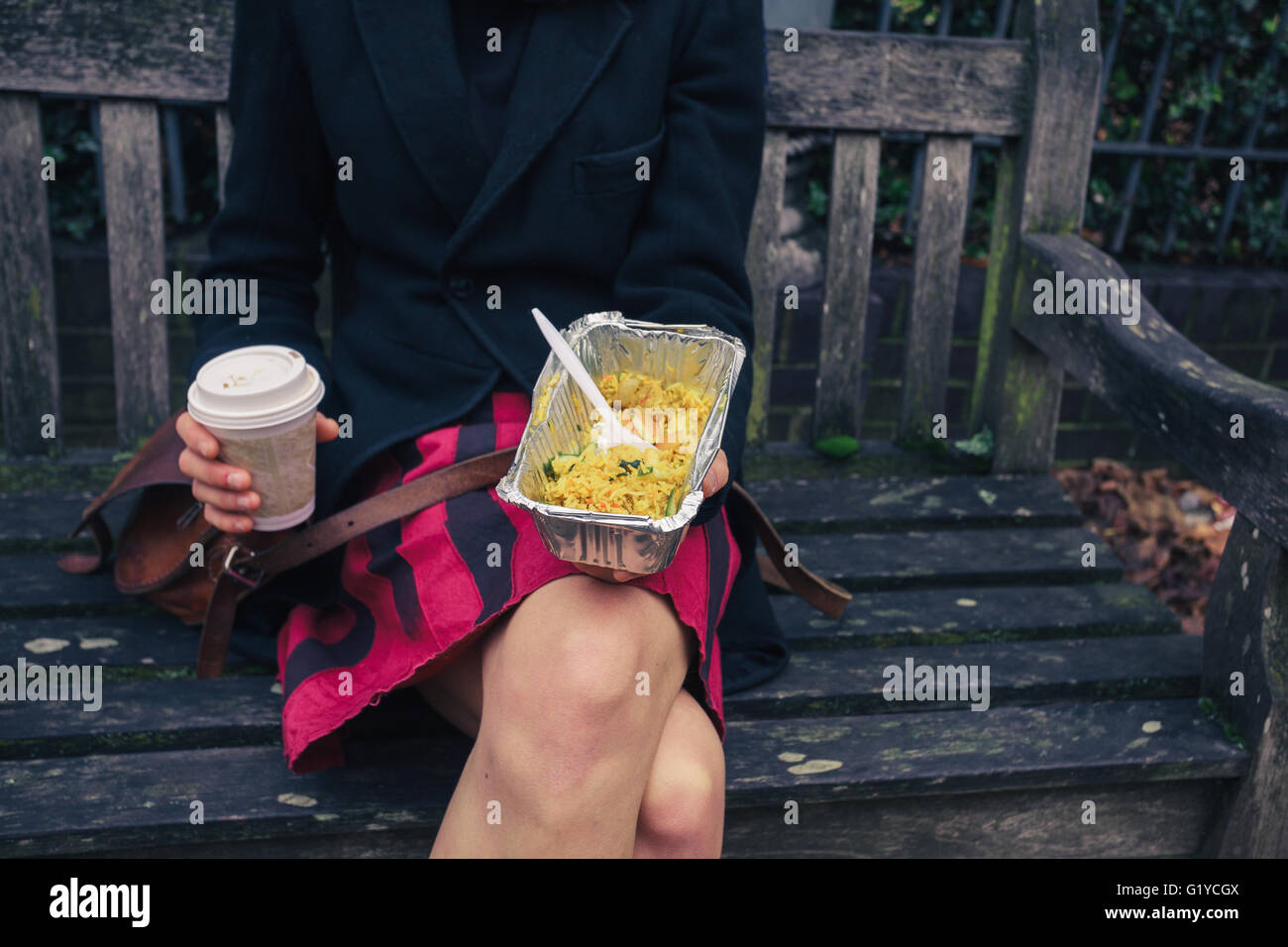 A woman i sitting on a bench and is holding a container of indian food ...